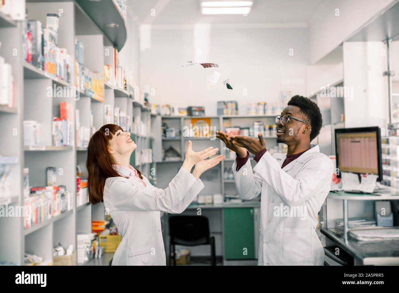 Two funny smiling young pharmacists having fun in pharmacy, throw up ...