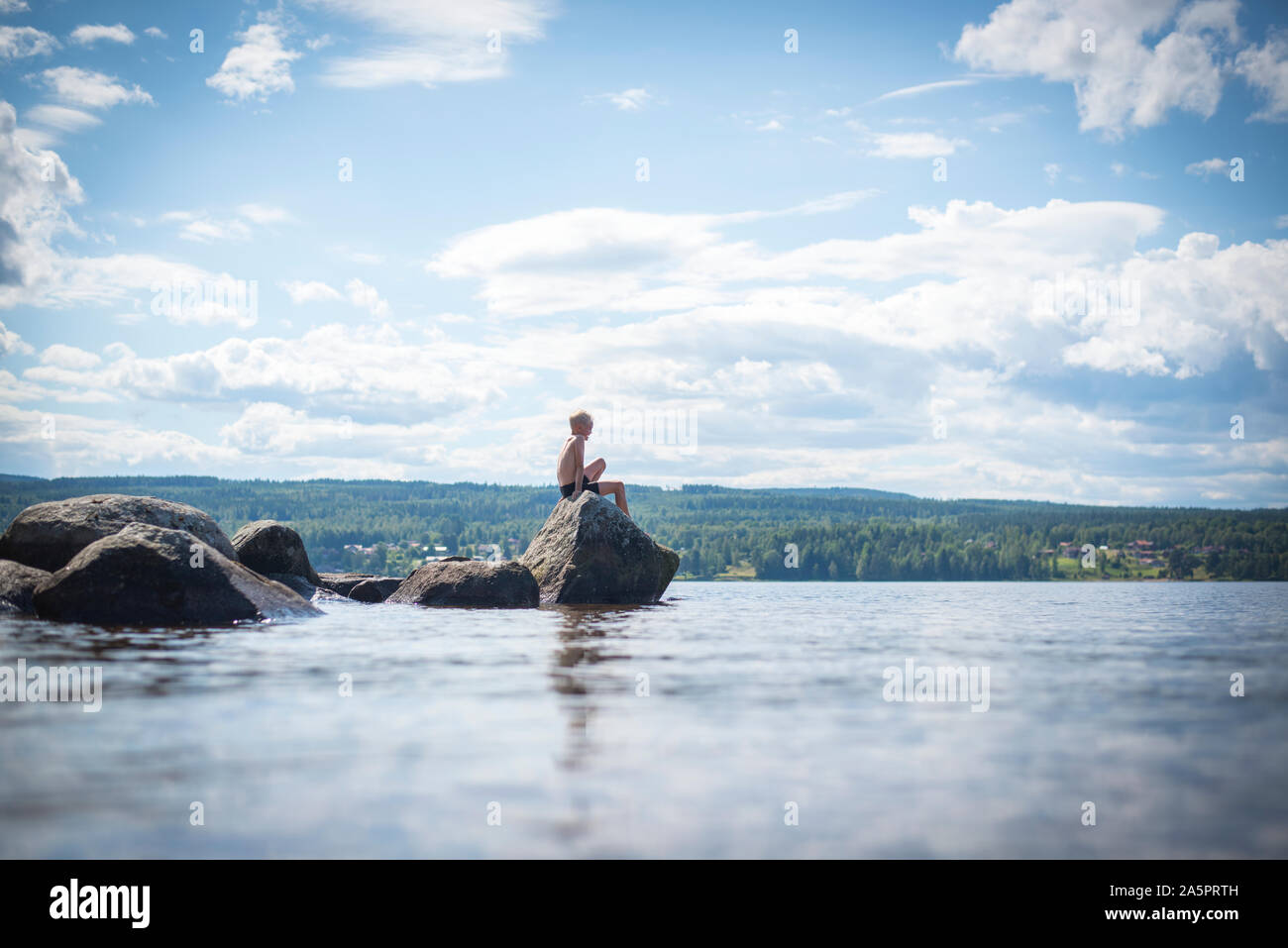 Boy sitting on rock at sea Stock Photo - Alamy