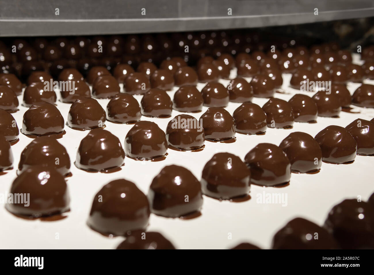 chocolates just poured with liquid chocolate, on a conveyor of a ...