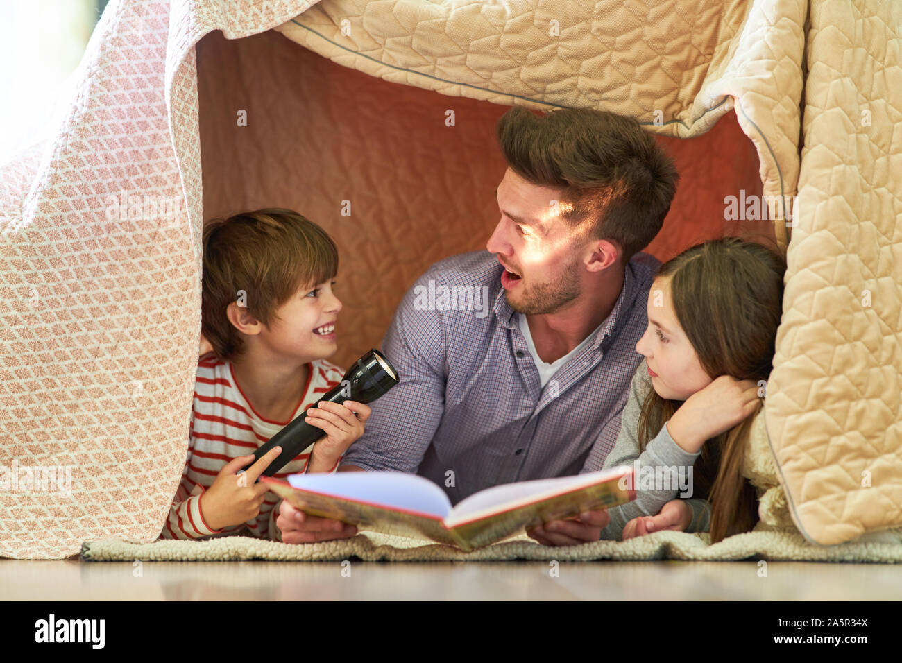 Father and two children reading a flashlight while reading a book under ...