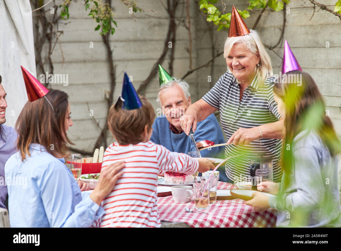 Happy extended family celebrates birthday with cake in the garden in ...
