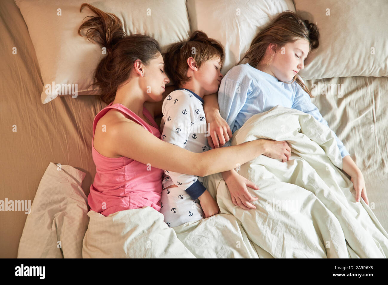 Mother cuddles with her two children in bed in the bedroom at home ...