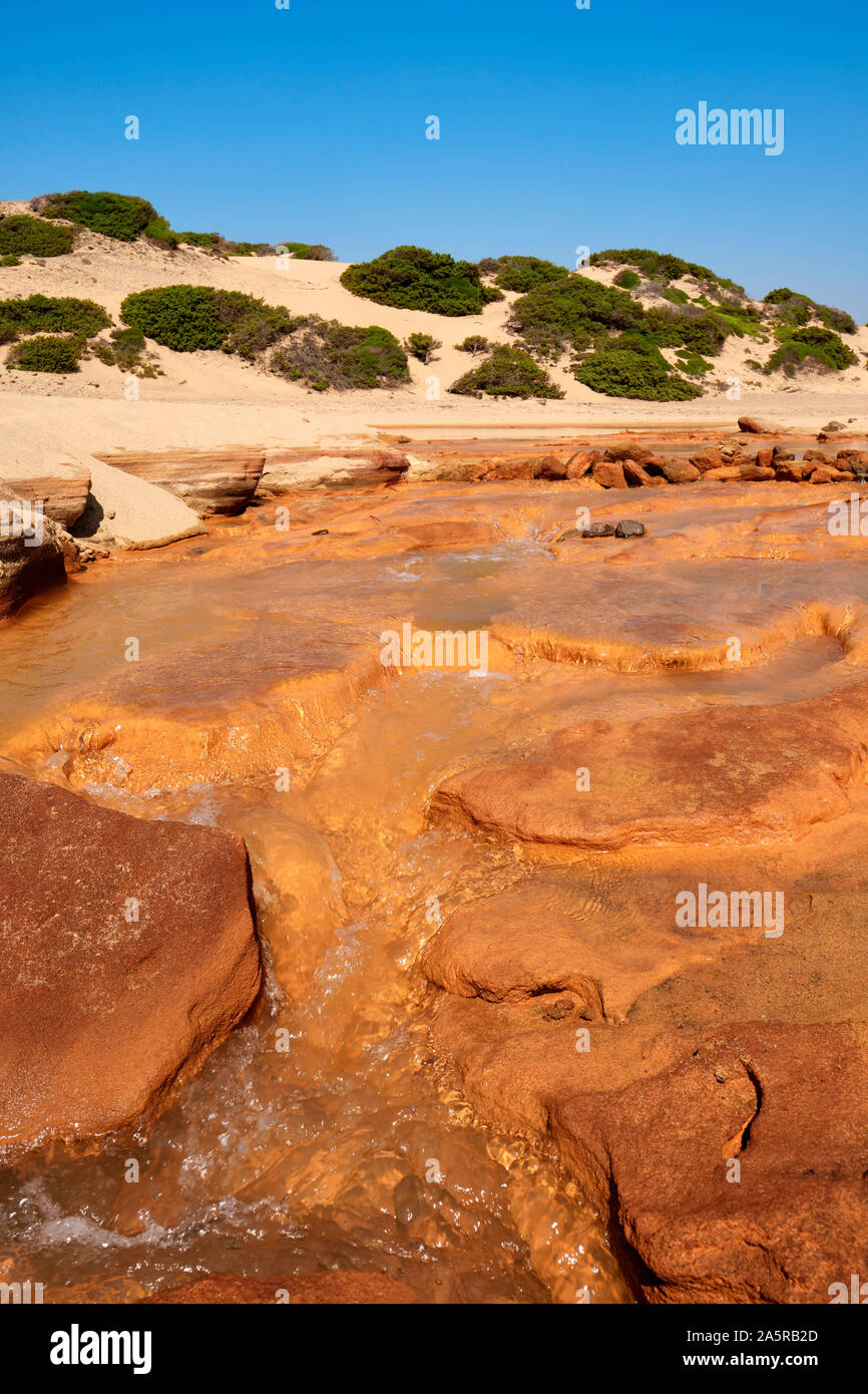 The red ochre mineral rich Piscinas river as it flows over the beach of ...