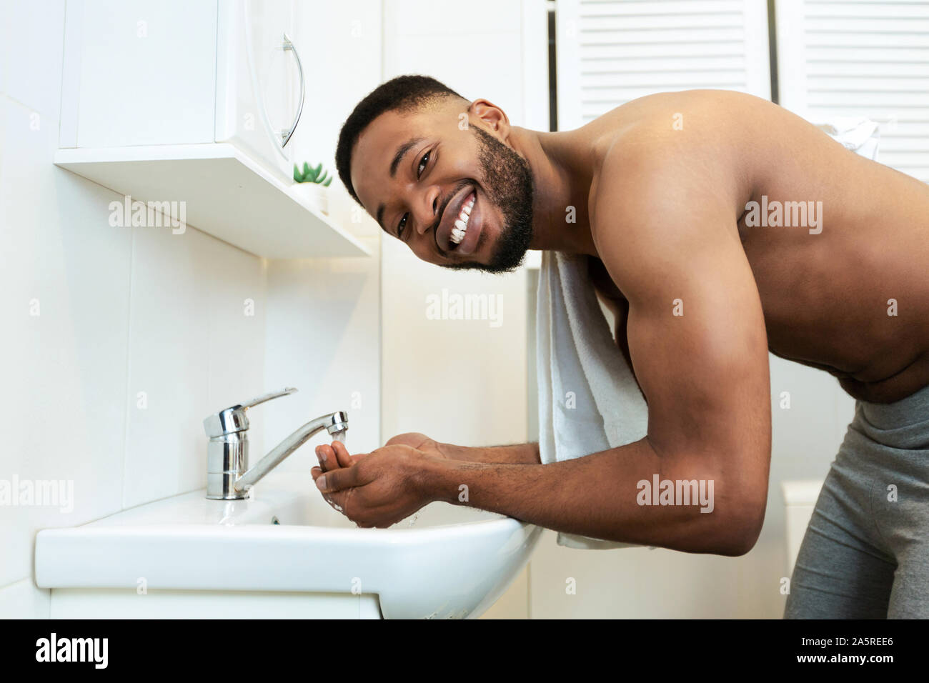 Shirtless african millennial man washing his face in bathroom Stock Photo - Alamy