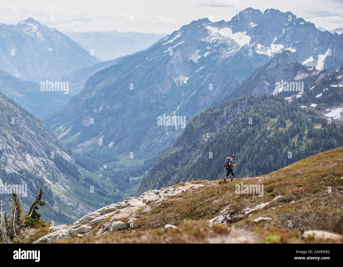 A male hiker walks on a trail with a view in the Cascades, Washington ...