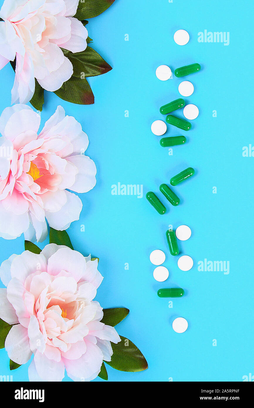 Capsules, pills and tablets with flowers on a blue table background ...