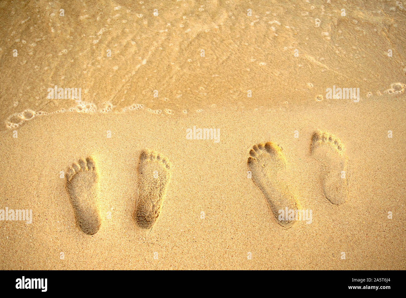 Feet prints on the sand of the beach and sea wave. Top view. Two people ...