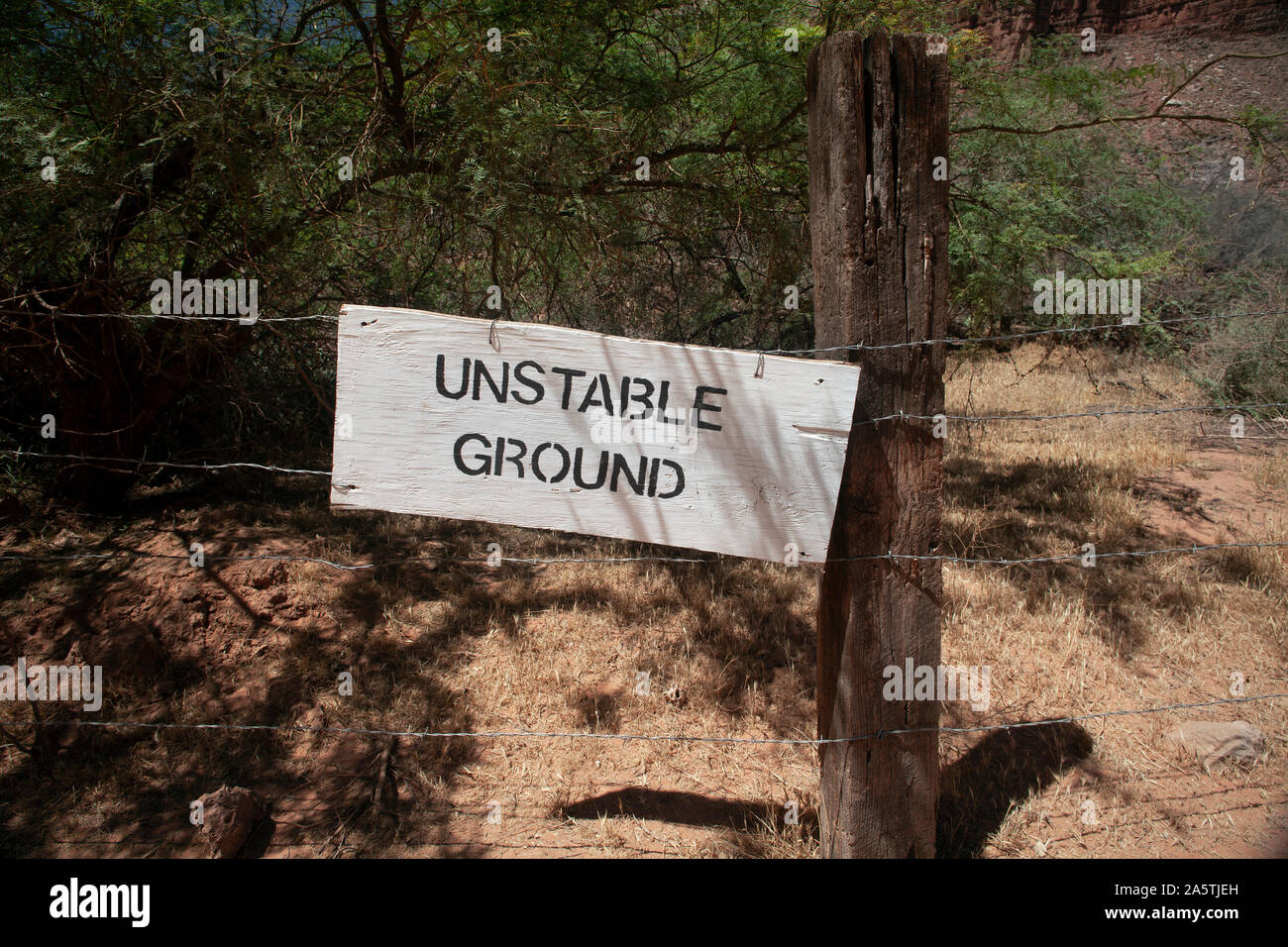 Wooden sign warning of unstable ground attached to barbed wire fence ...