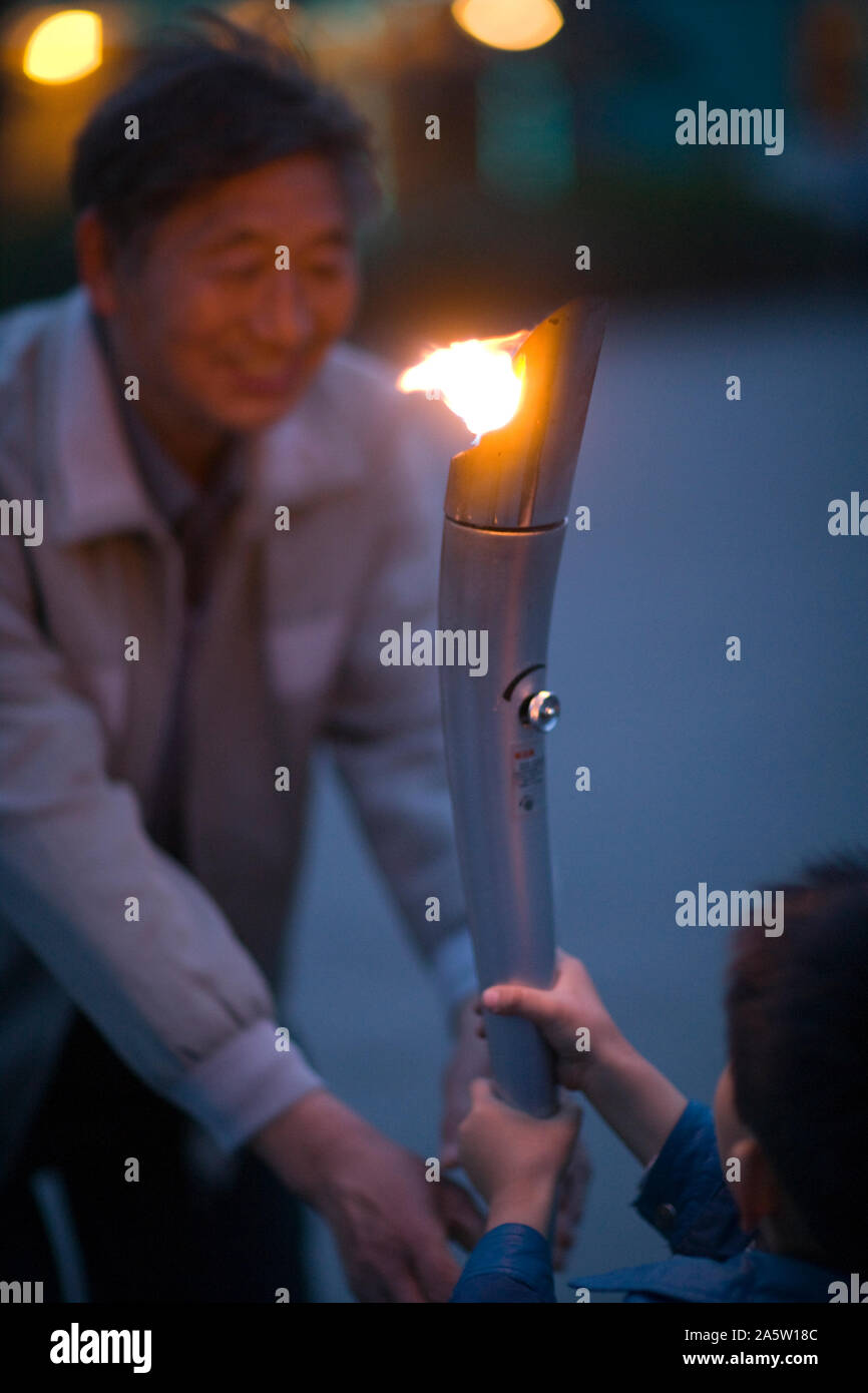 Young boy handing an Olympic torch to his mature grandfather in a park ...