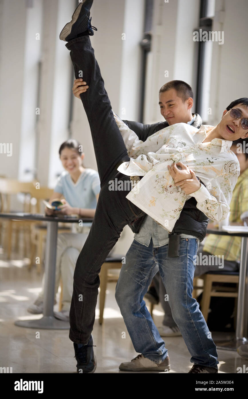 Teenage boy lifting the leg of a male friend while holding his waist in ...