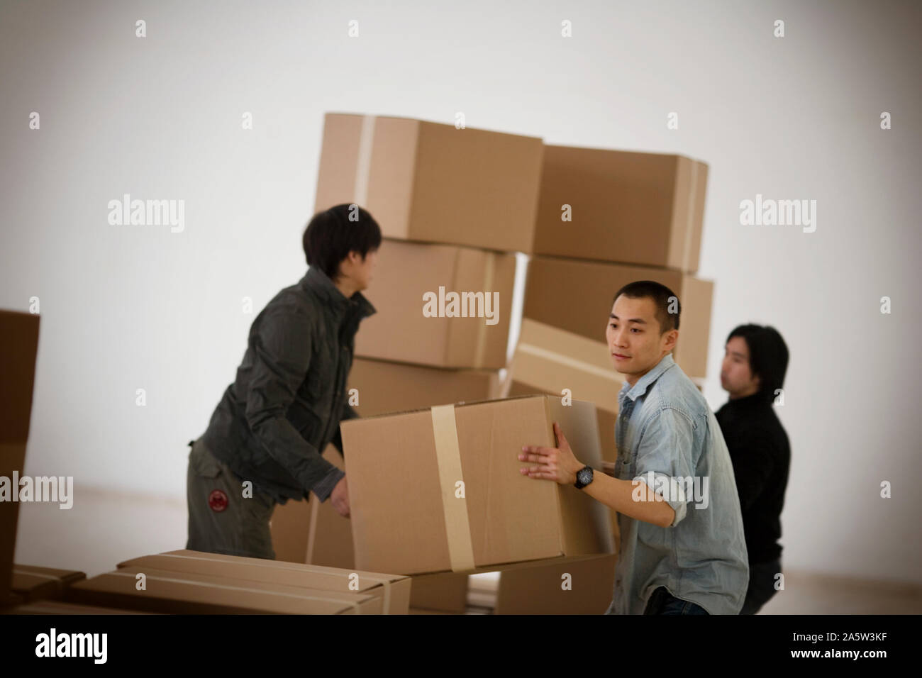 Three young adult men stacking boxes to carry Stock Photo - Alamy