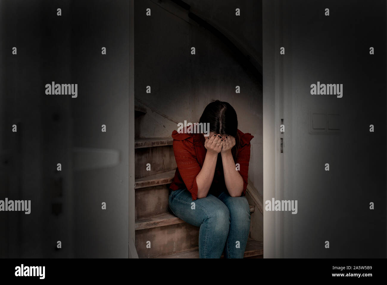 Young woman cries and sitting on a stairs in the dark, lonely sad and ...