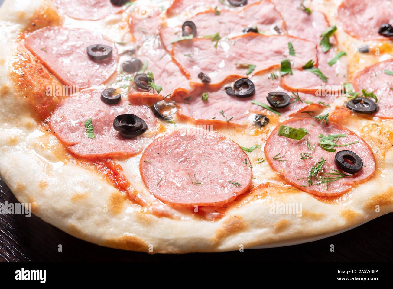 Cheap pizza with pepperoni, ham, olives and herbs Stock Photo - Alamy