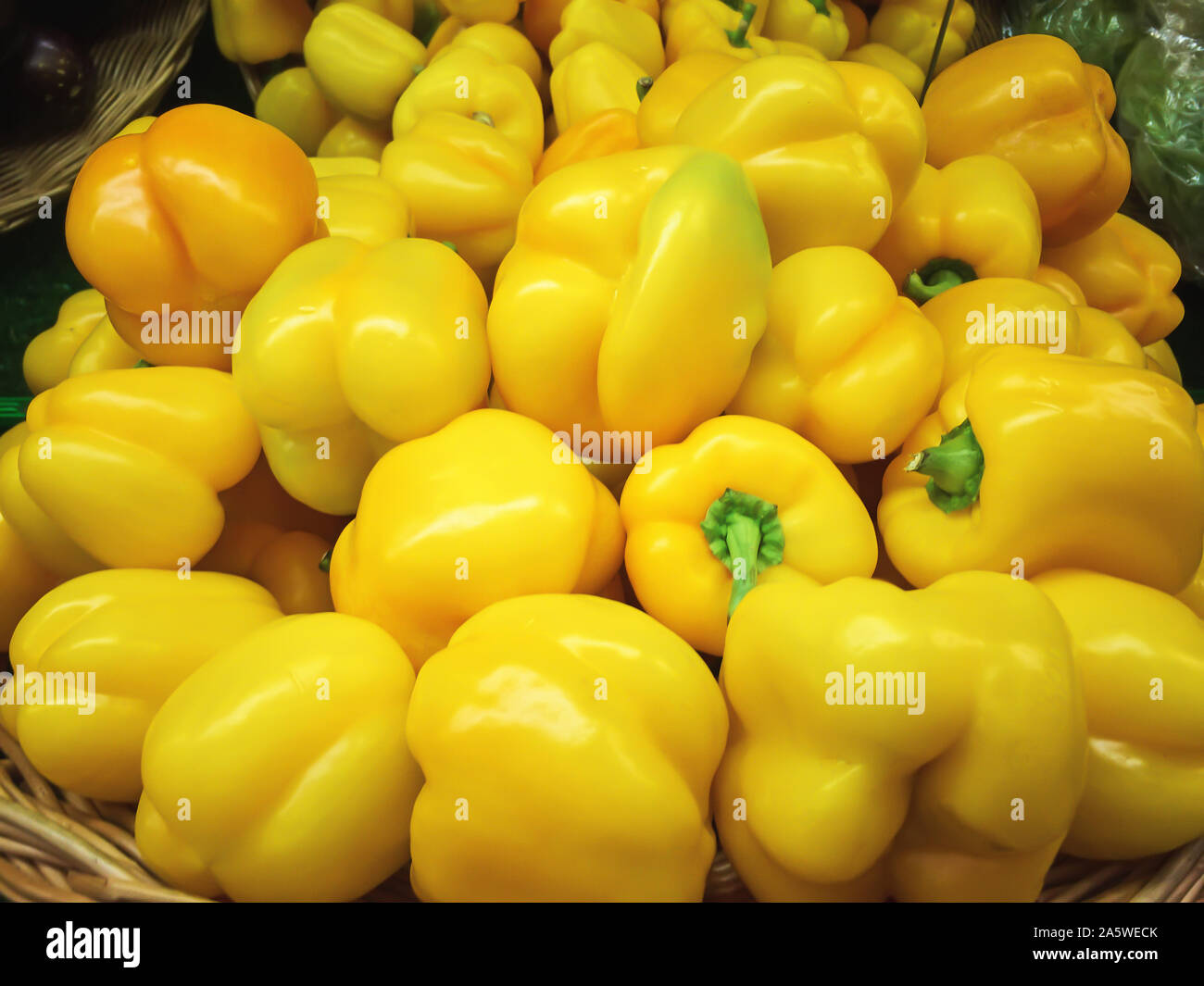 Fresh yellow peppers on a wicker plate in the store with lens flare ...