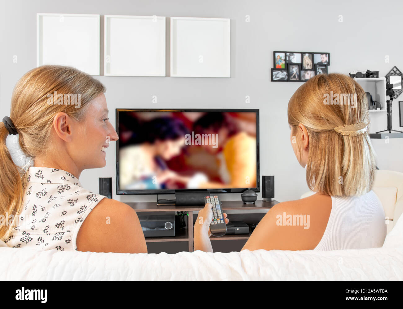 Young women sitting on couch holding remote control enjoying watching ...