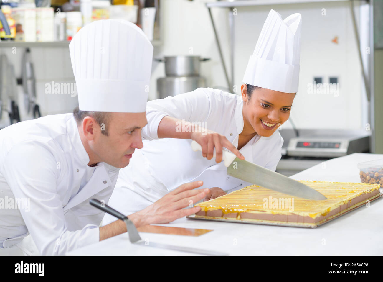 master chef guiding trainee cutting large dessert Stock Photo - Alamy