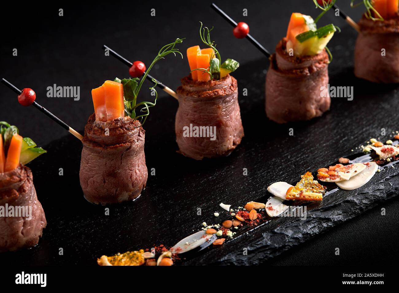 Mini roast beef rolls with vegetables, on a black slate plate, on a ...