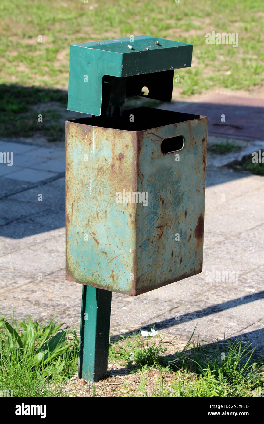 Dilapidated partially rusted green metal trash can with faded color ...
