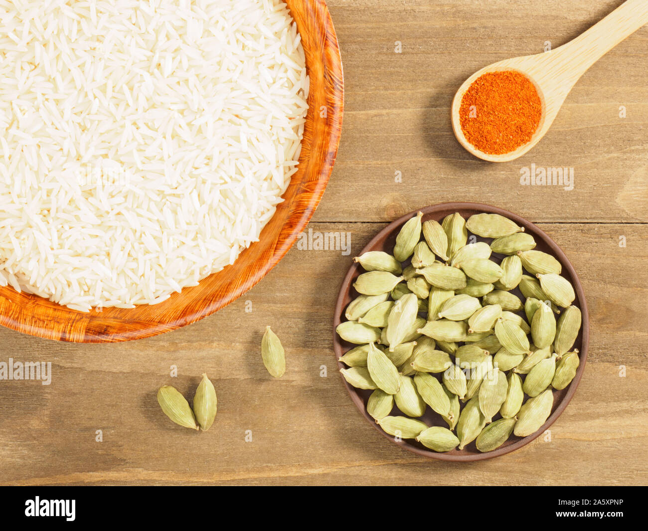 Rice, green cardamom, chili pepper on brown wooden background. Indian ...