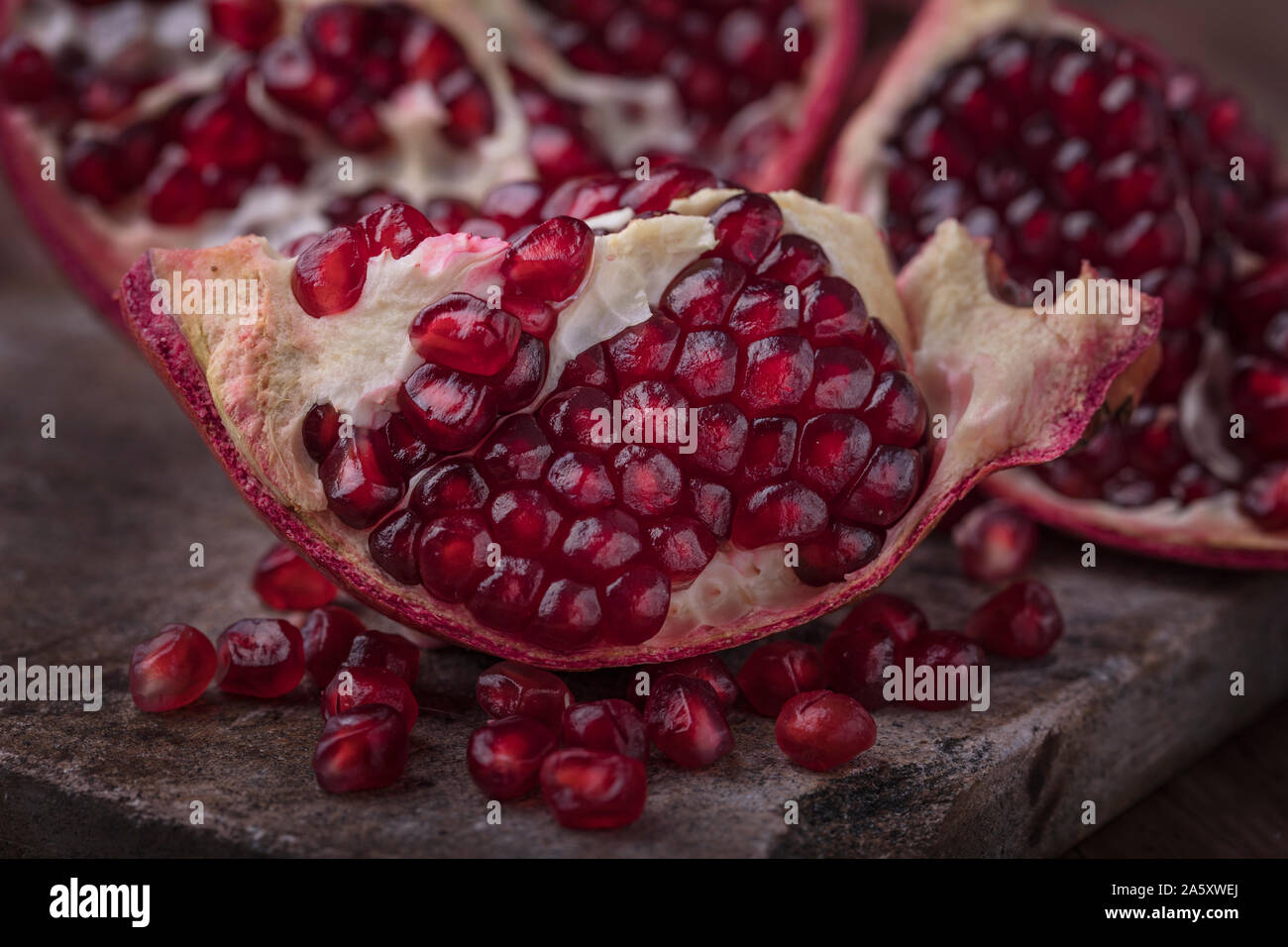 Pomegranate slices. The fruits are on a rustic stone surface and there ...