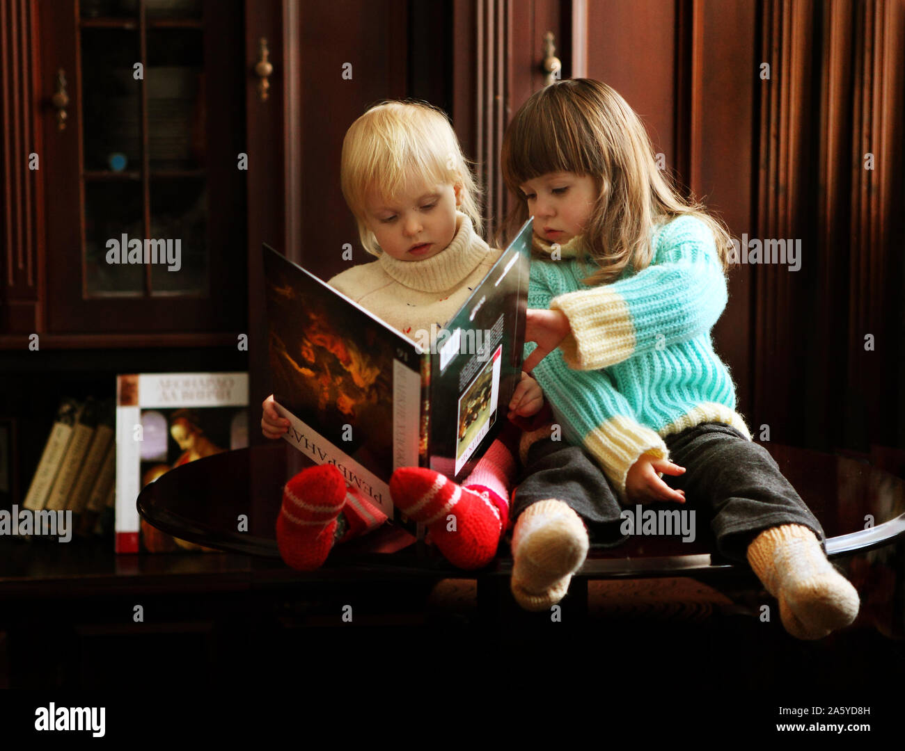 Two little girls are reading a book Stock Photo - Alamy