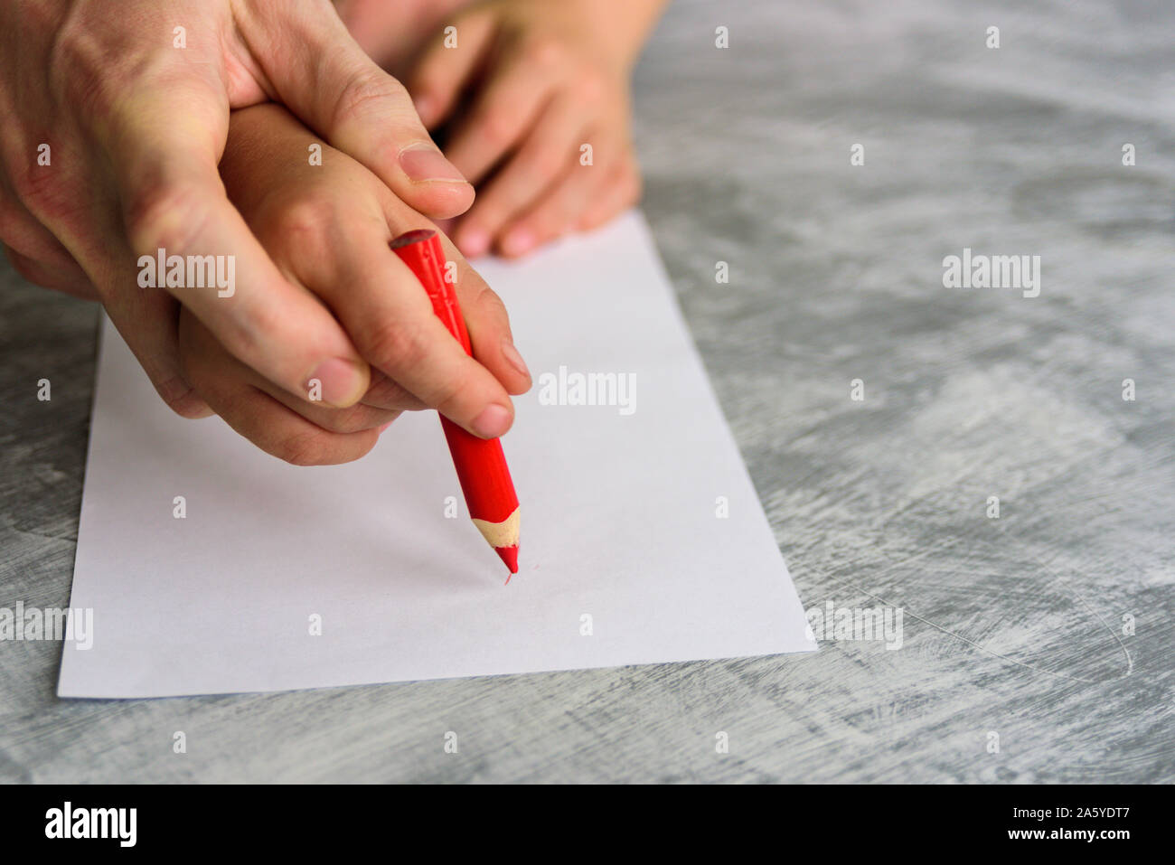 Father teaching child to write letters with his hands. Red pencil and ...