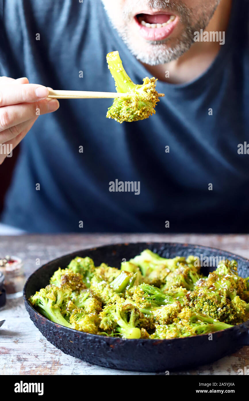 A man puts broccoli in his mouth with chopsticks. Cooking broccoli ...