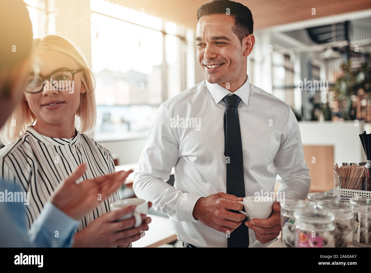Smiling young businessman talking with two female colleagues during ...