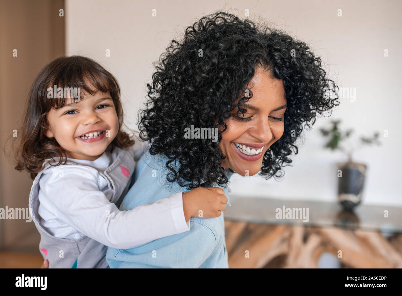 Laughing mother piggybacking her cute daughter around the house Stock ...