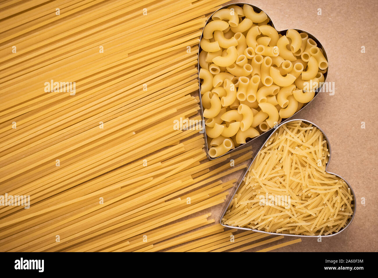 Two hearts of pasta on brown paper background. Heap of raw spaghetti on ...
