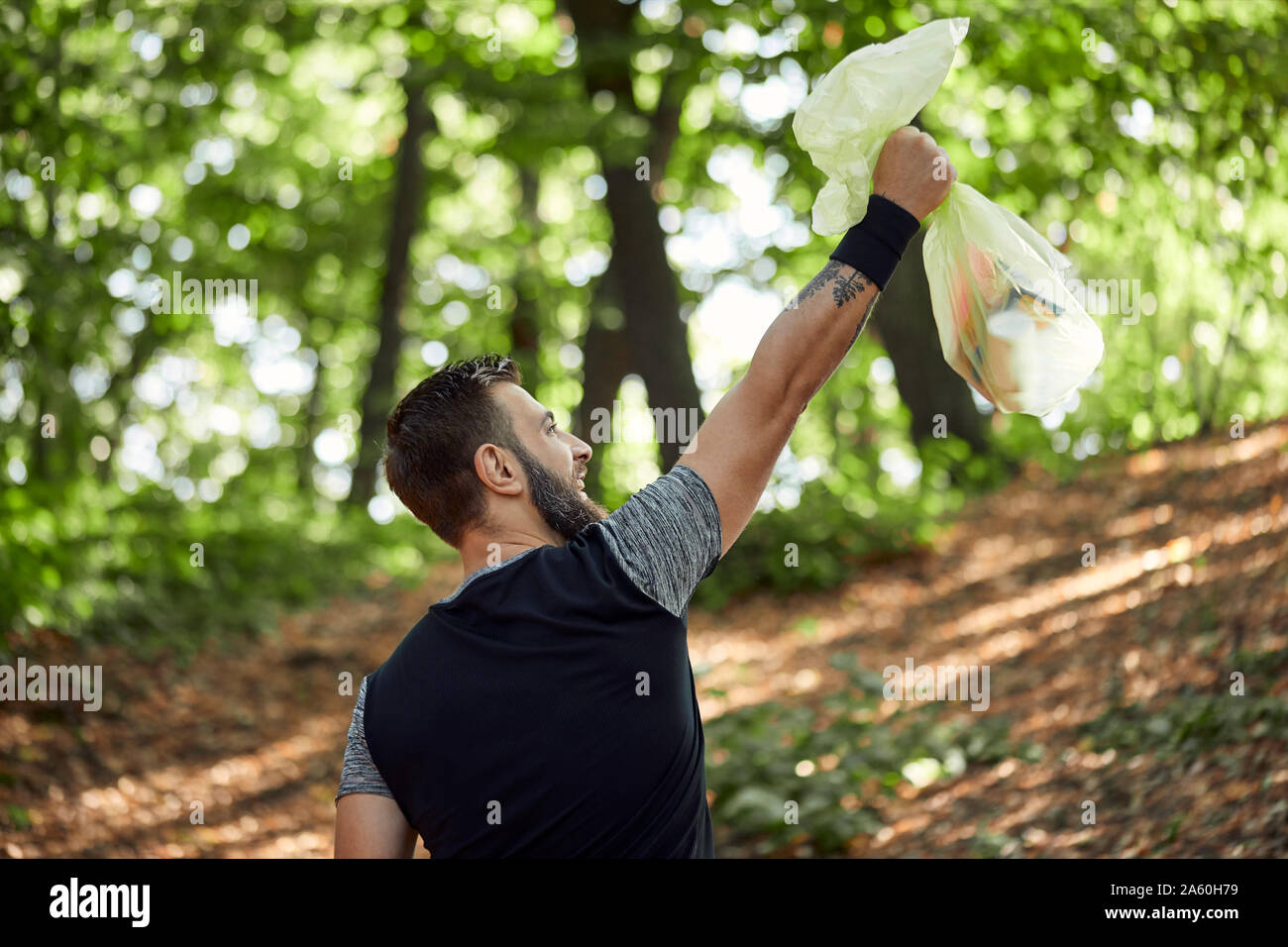 Sporty man holding litter bag in forest Stock Photo - Alamy