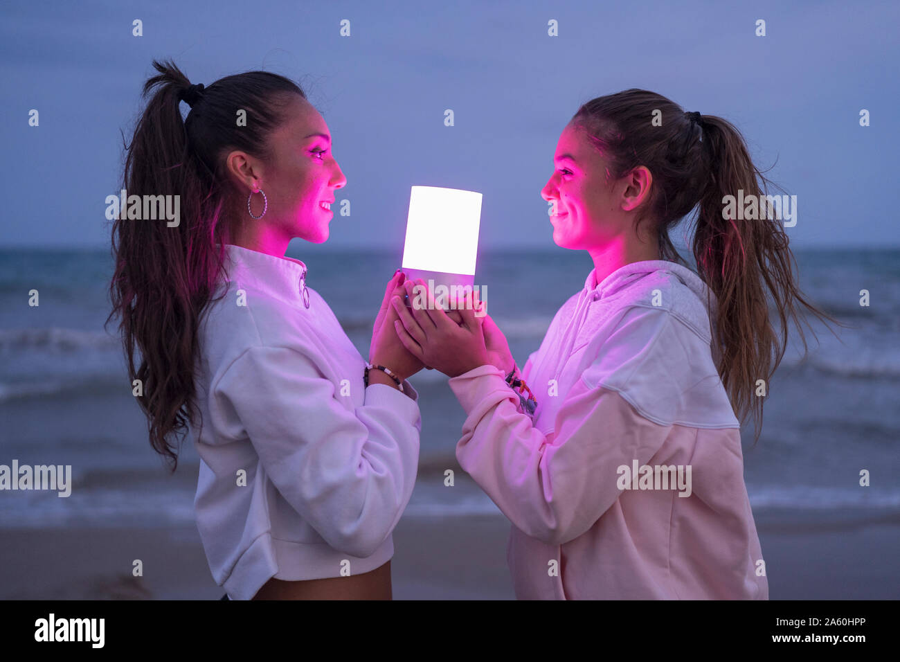 Two female friends holding led light on the beach at night Stock Photo ...