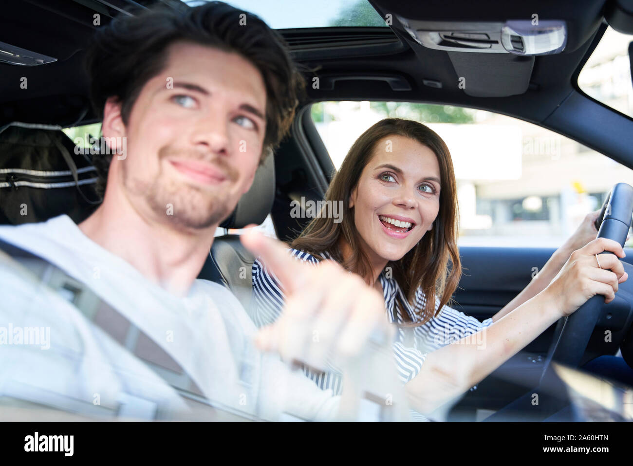 Happy couple in a car with woman driving and man pointing his finger ...