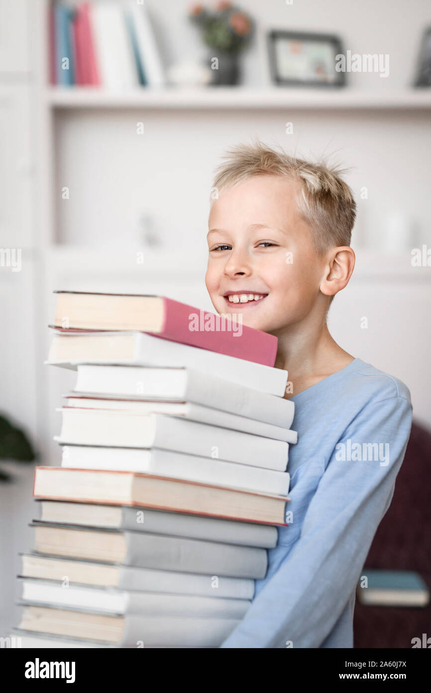 Portrait of smiling blond boy carrying stack of books Stock Photo - Alamy