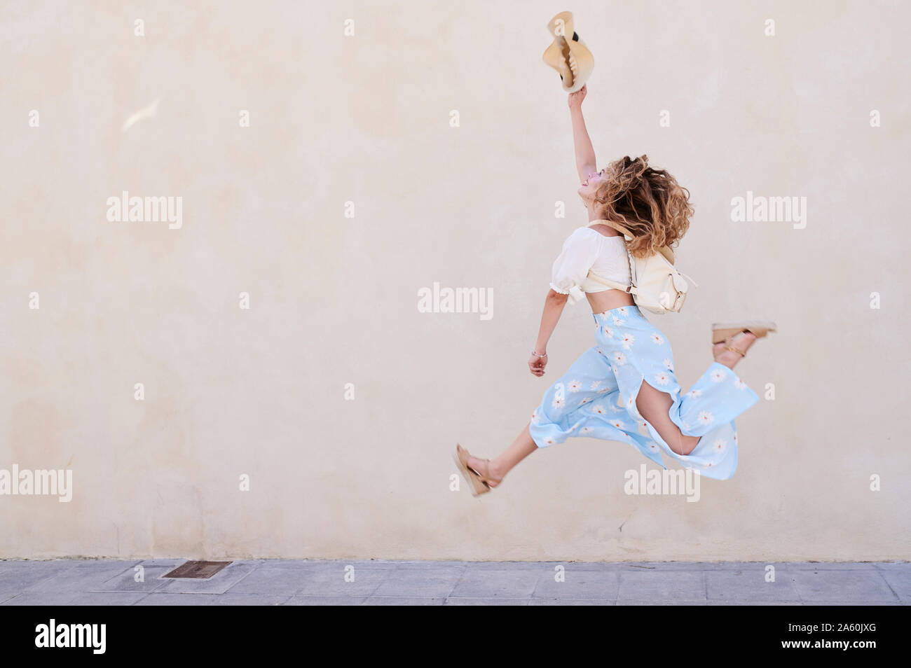 Carefree young woman with hat jumping at a wall Stock Photo - Alamy