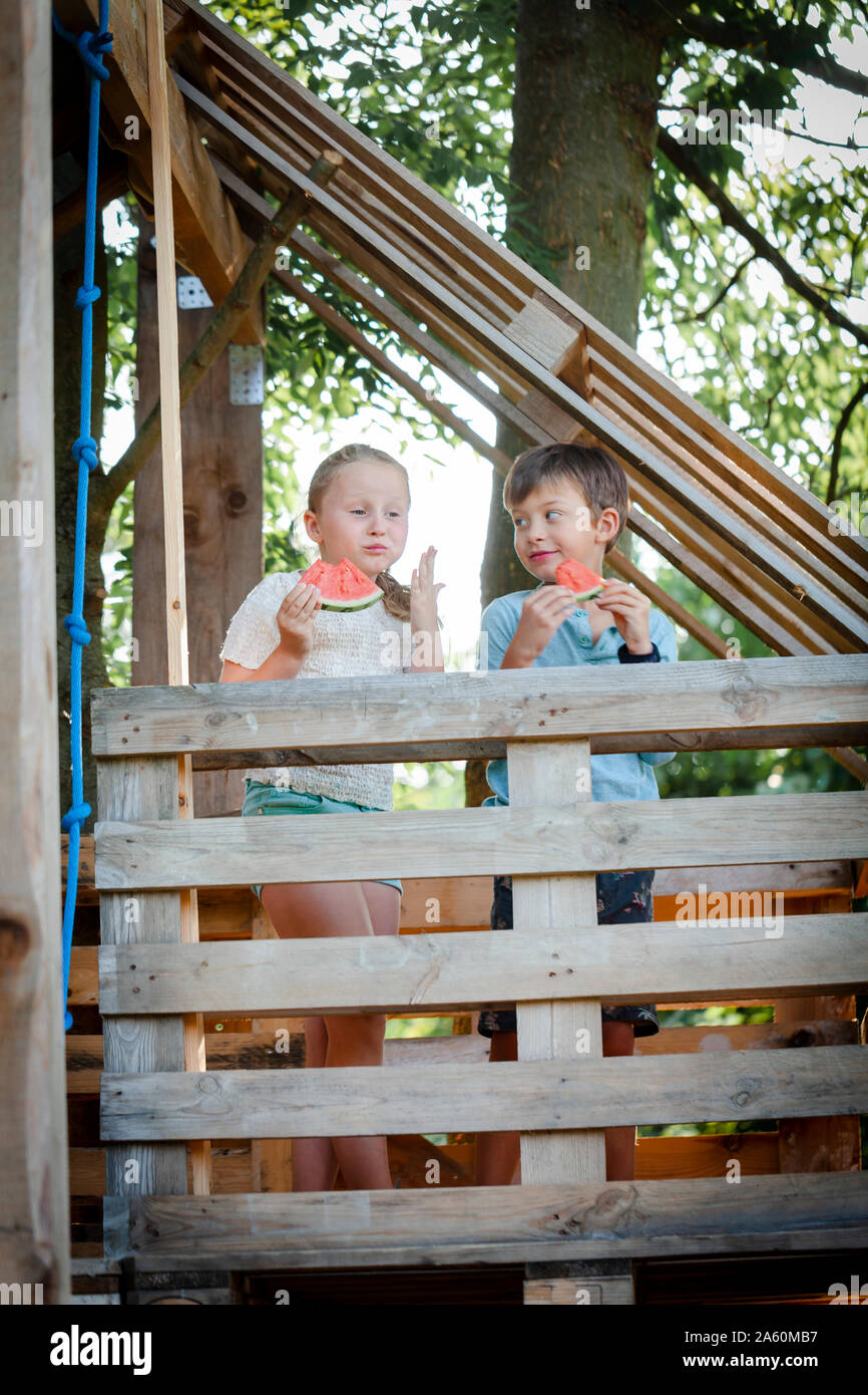Girl and boy eating watermelon in tree house Stock Photo - Alamy
