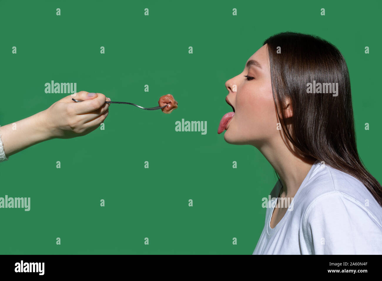 Hand feeding young woman in front of green background Stock Photo - Alamy