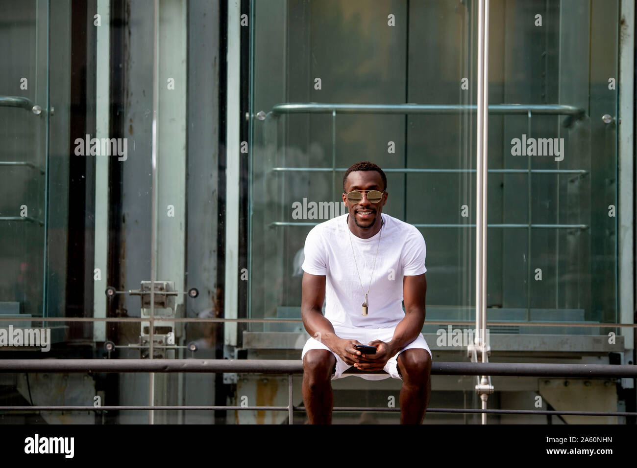 Young smiling man sitting on railing and using smartphone Stock Photo ...