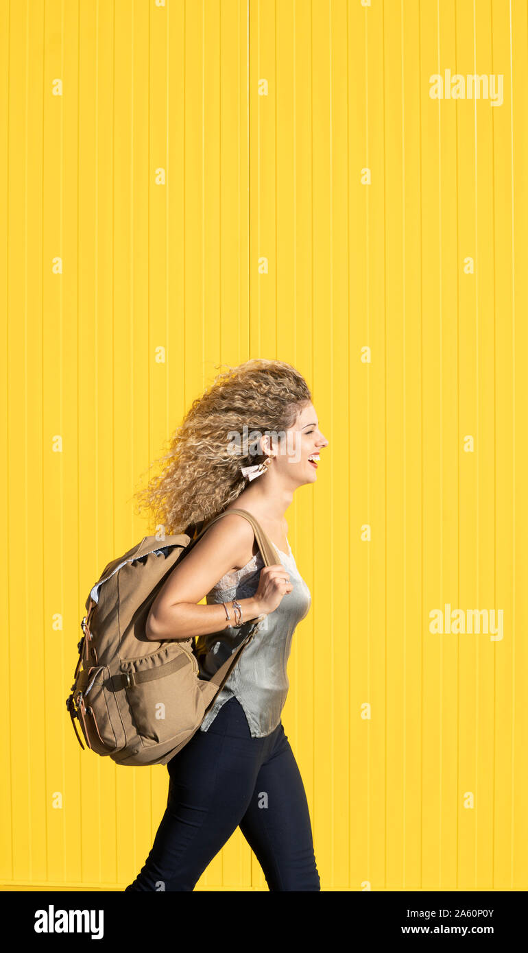 Young woman carrying backpack in front of yellow background Stock Photo ...