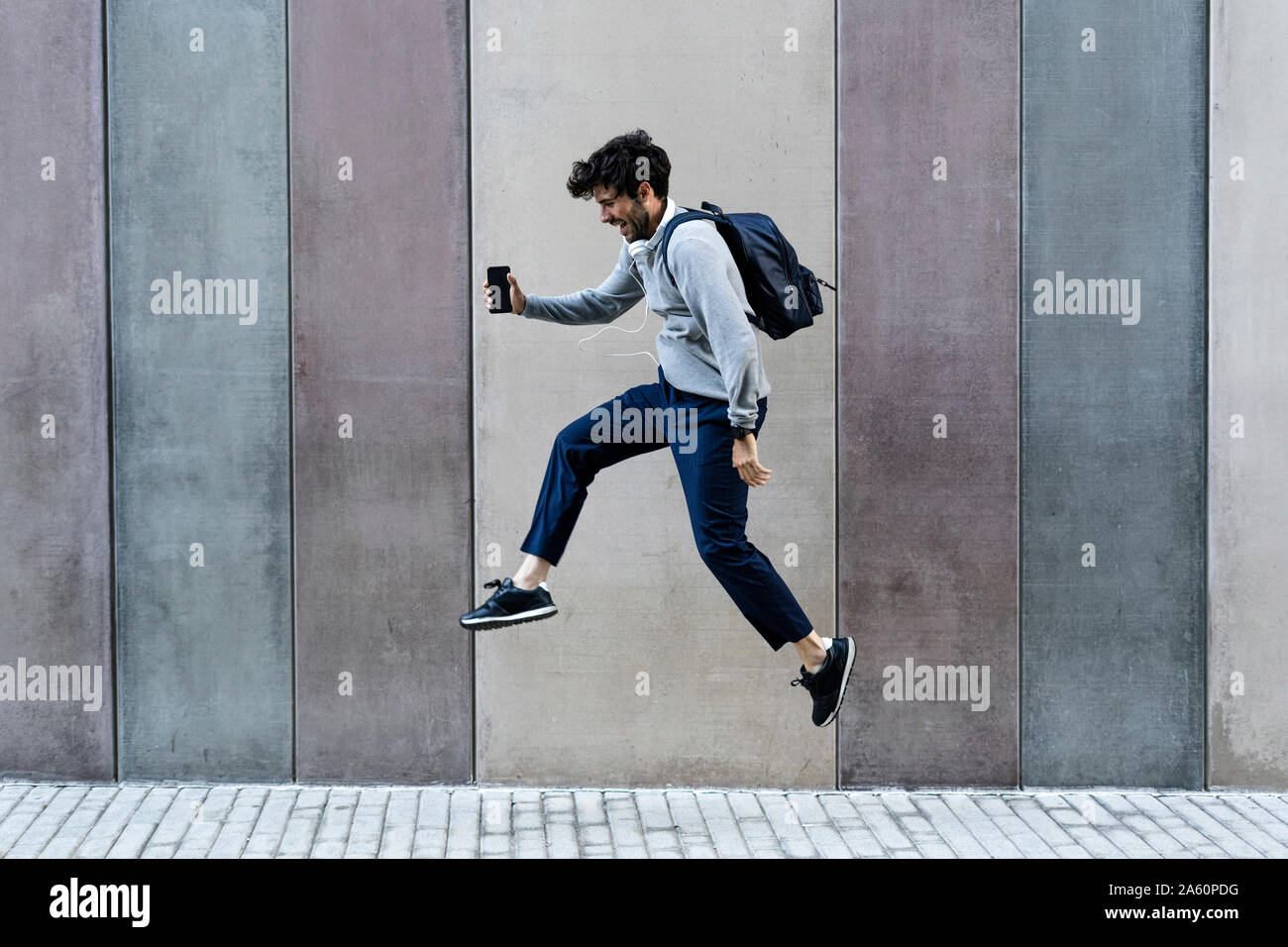 Happy man holding cell phone jumping in front of a wall Stock Photo - Alamy