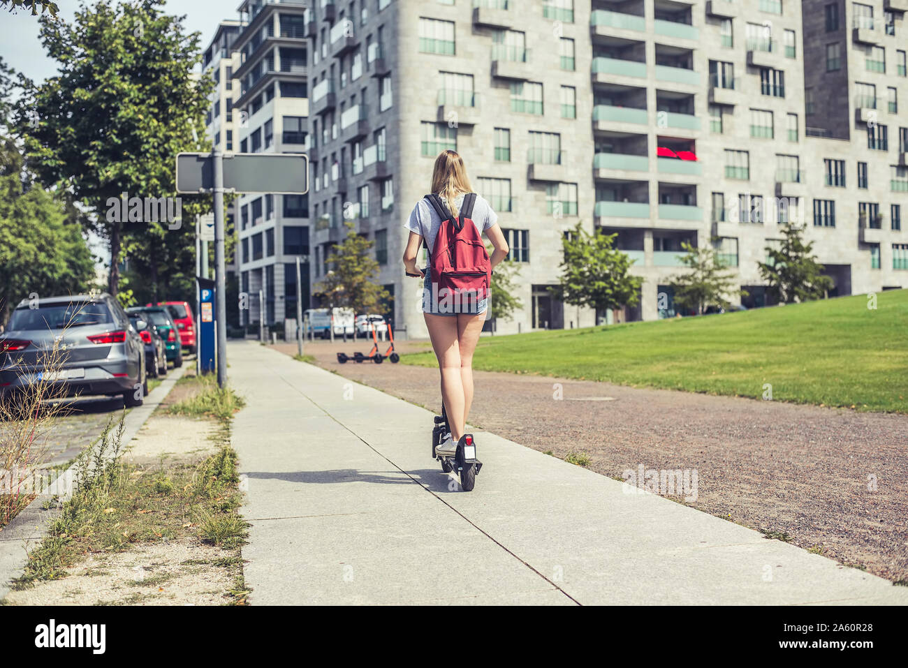 Back view of young woman with backpack riding E-Scooter on pavement ...