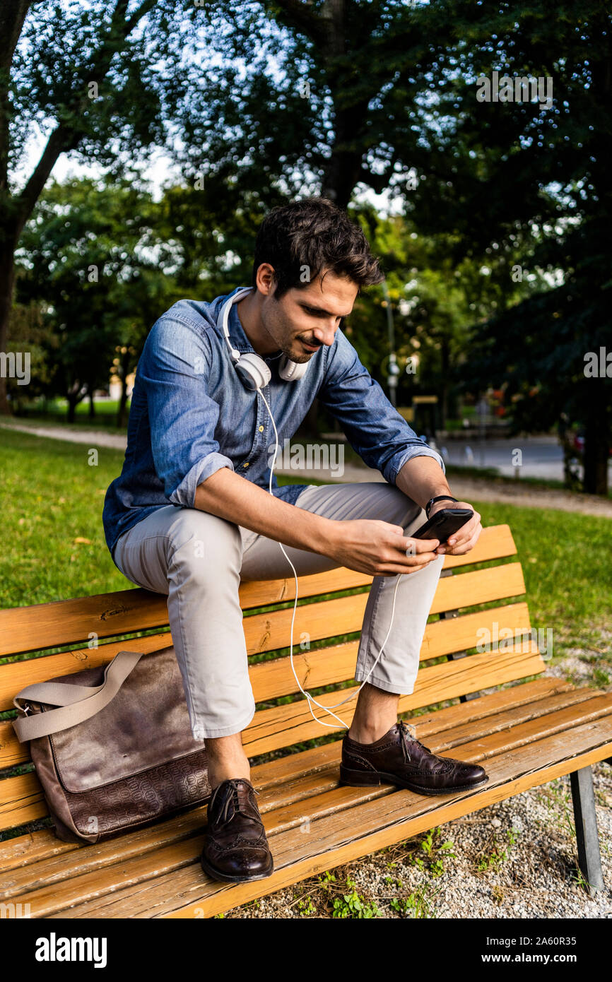 Smiling man sitting on a park bench using his smartphone Stock Photo ...