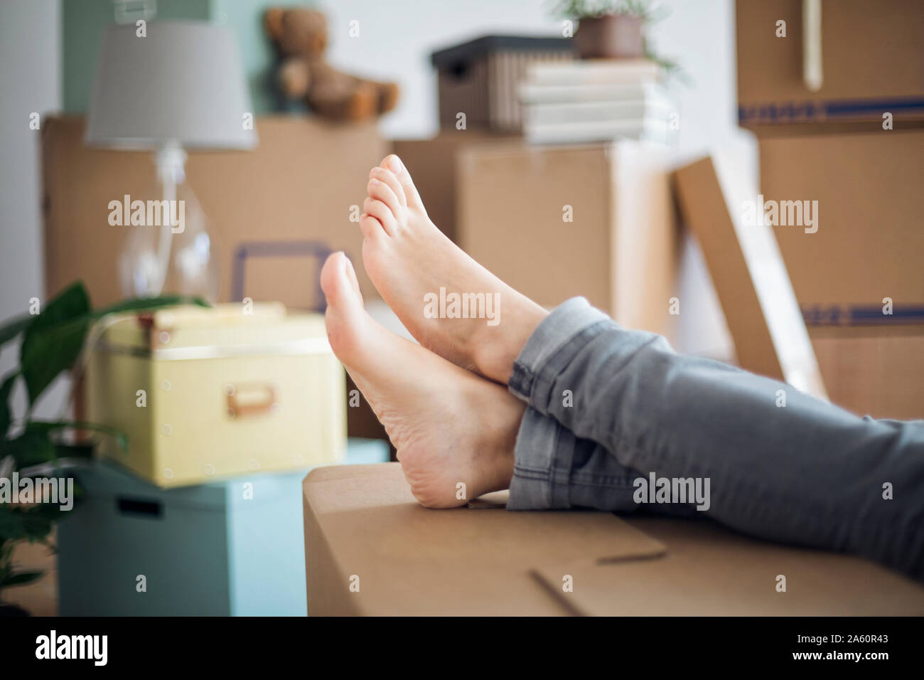 Bare feet of woman relaxing surrounded by cardboard boxes in a new home ...