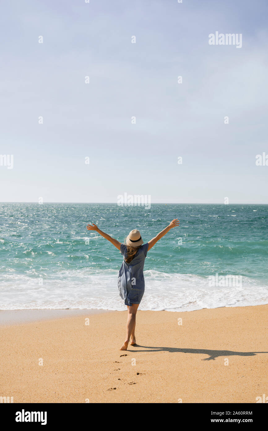 Rear view of woman raising her arms on the beach hi-res stock ...