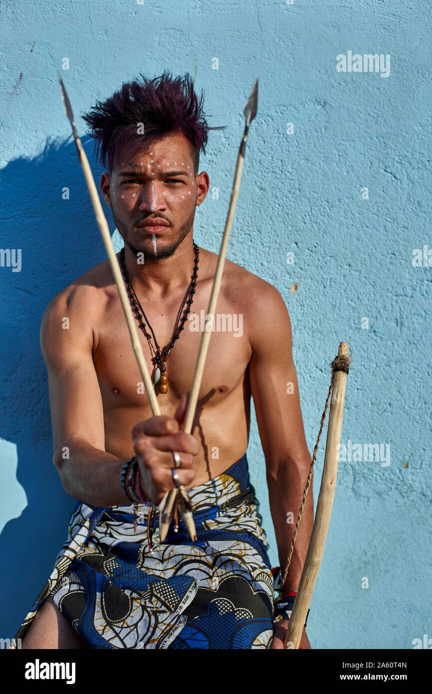 Tribal man with his traditional arch and arrows leaning on blue wall ...