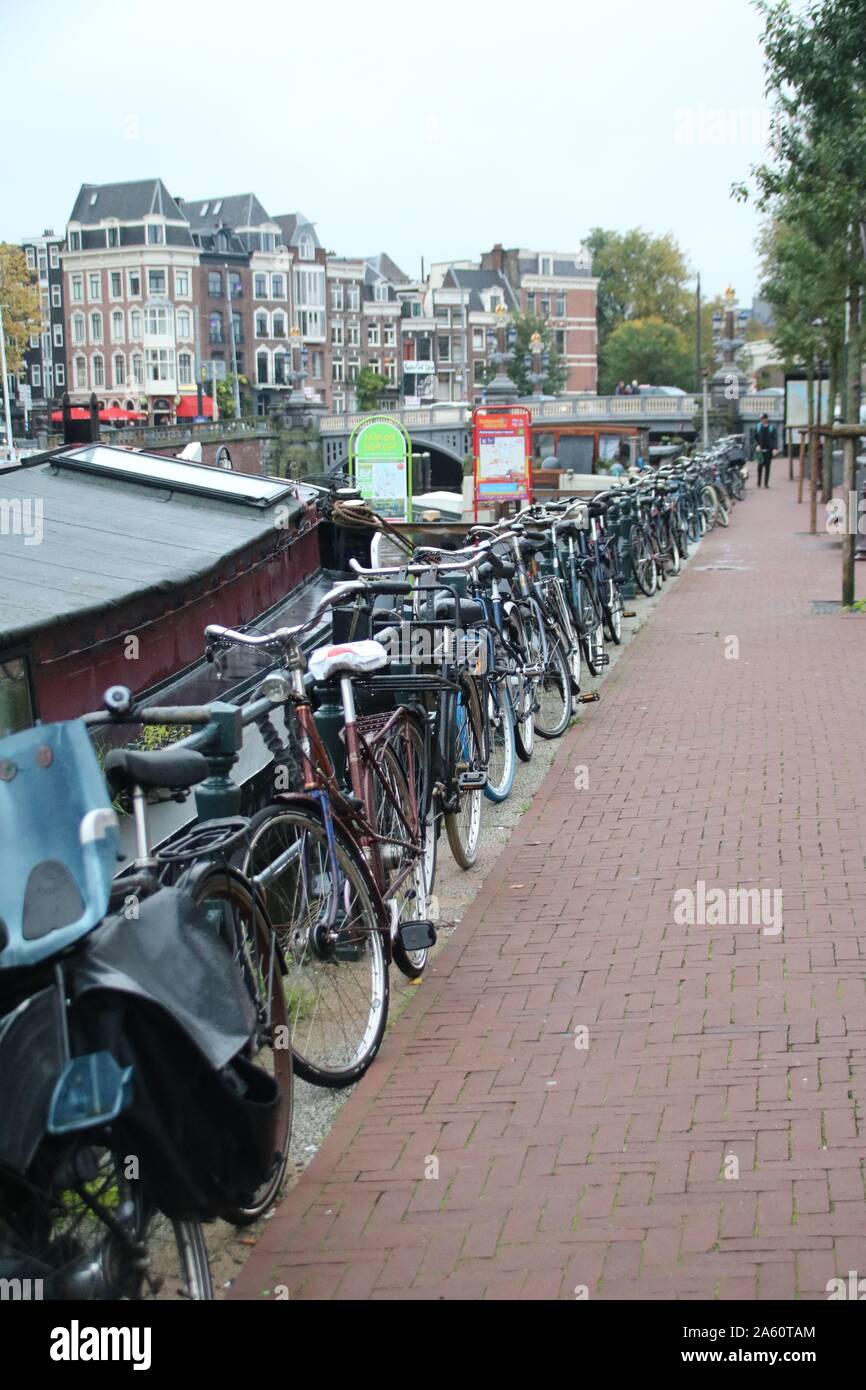 a long line of bikes locked to railings next to an Amsterdam canal ...