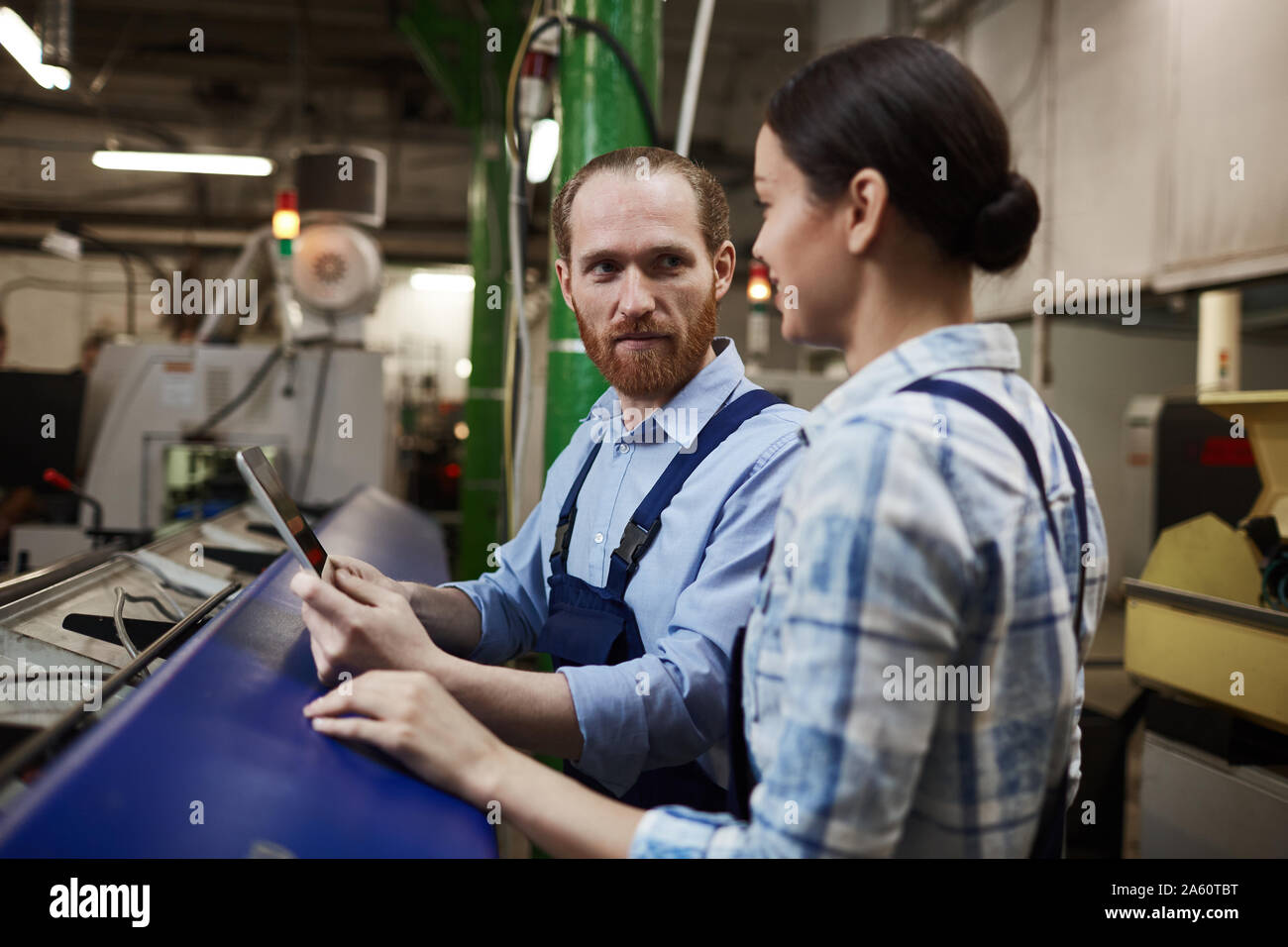 Two engineers in overalls using digital tablet and talking to each ...