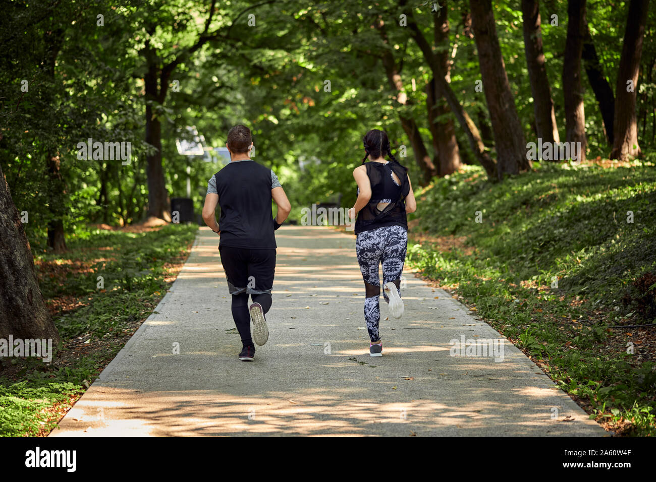 Rear view of sporty couple running on forest path Stock Photo - Alamy