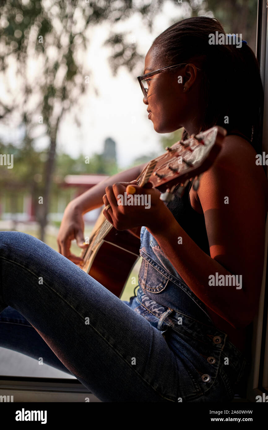 Woman playing guitar sitting at the edge of the window Stock Photo - Alamy