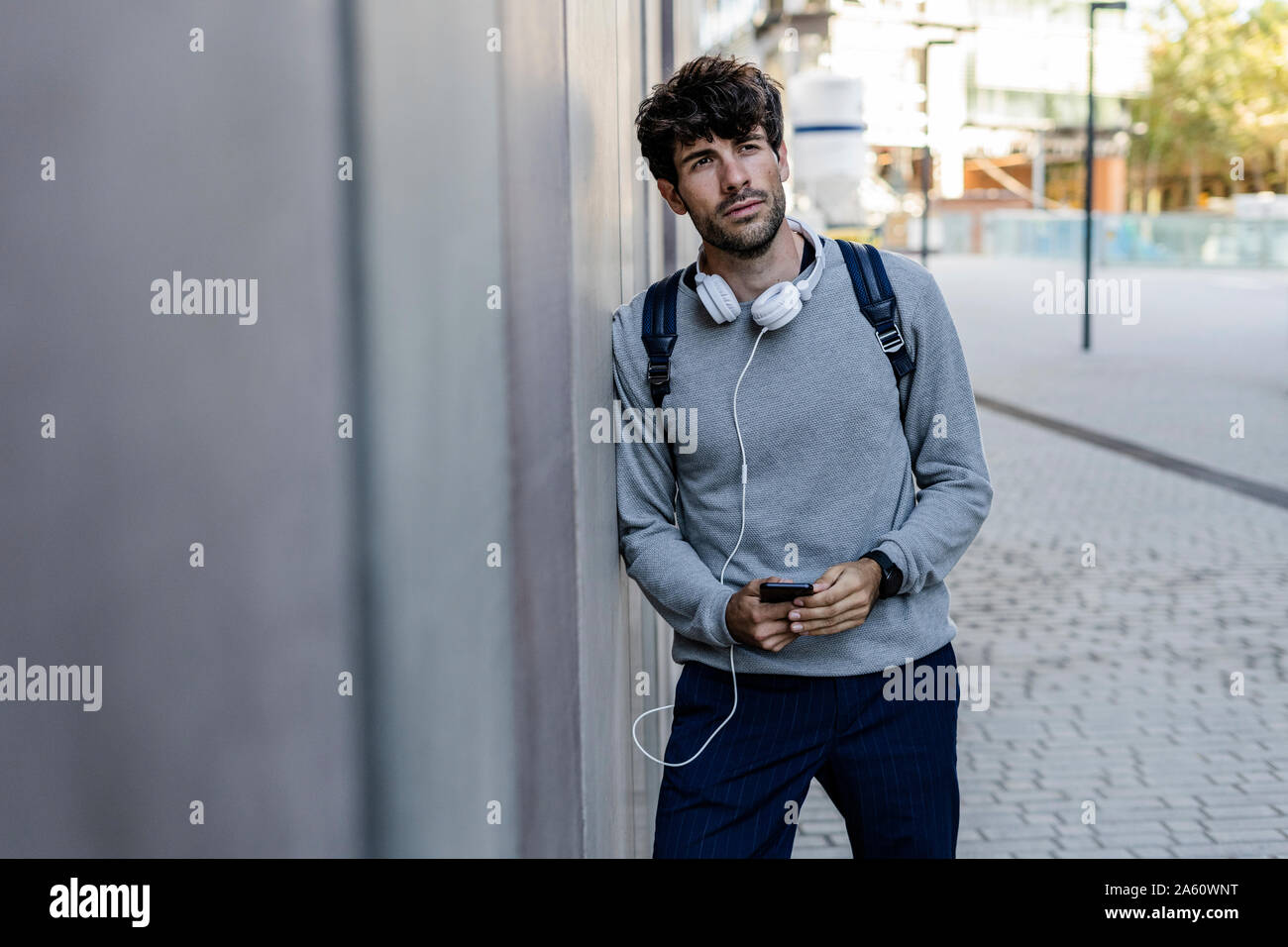 Man holding cell phone leaning against a wall Stock Photo - Alamy